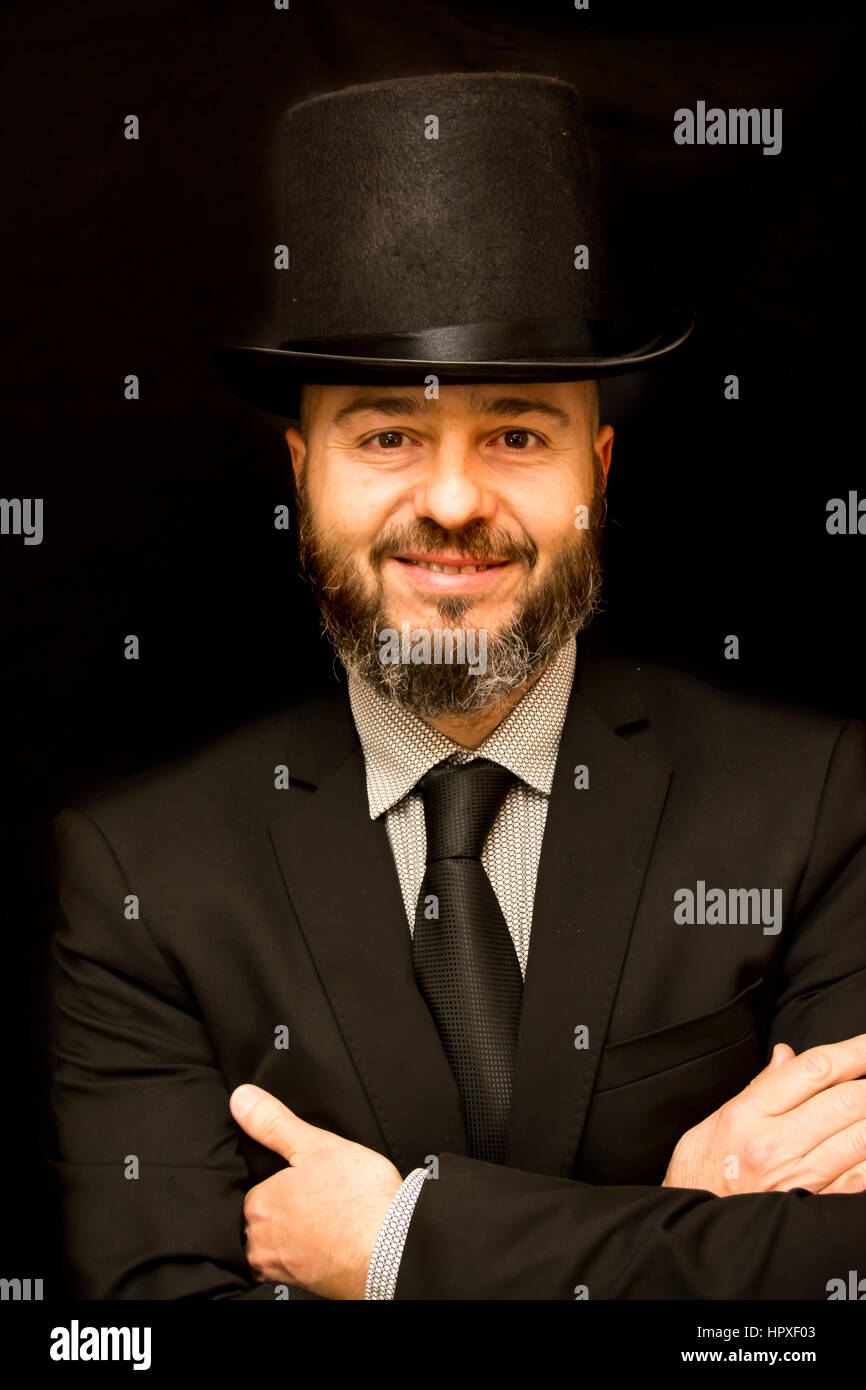 Handsome, bald man with beard, suit, tie and hat, on black background ...