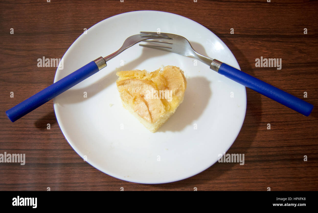 Piece of apple pie with heart shape and two forks interlaced on a ...