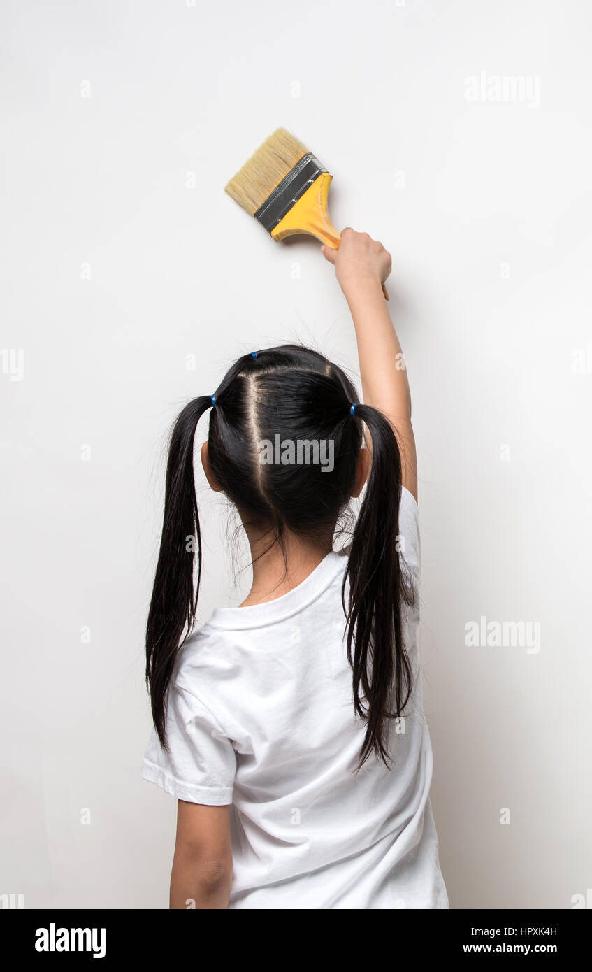 Little girl drawing something using painting brush on wall background ...