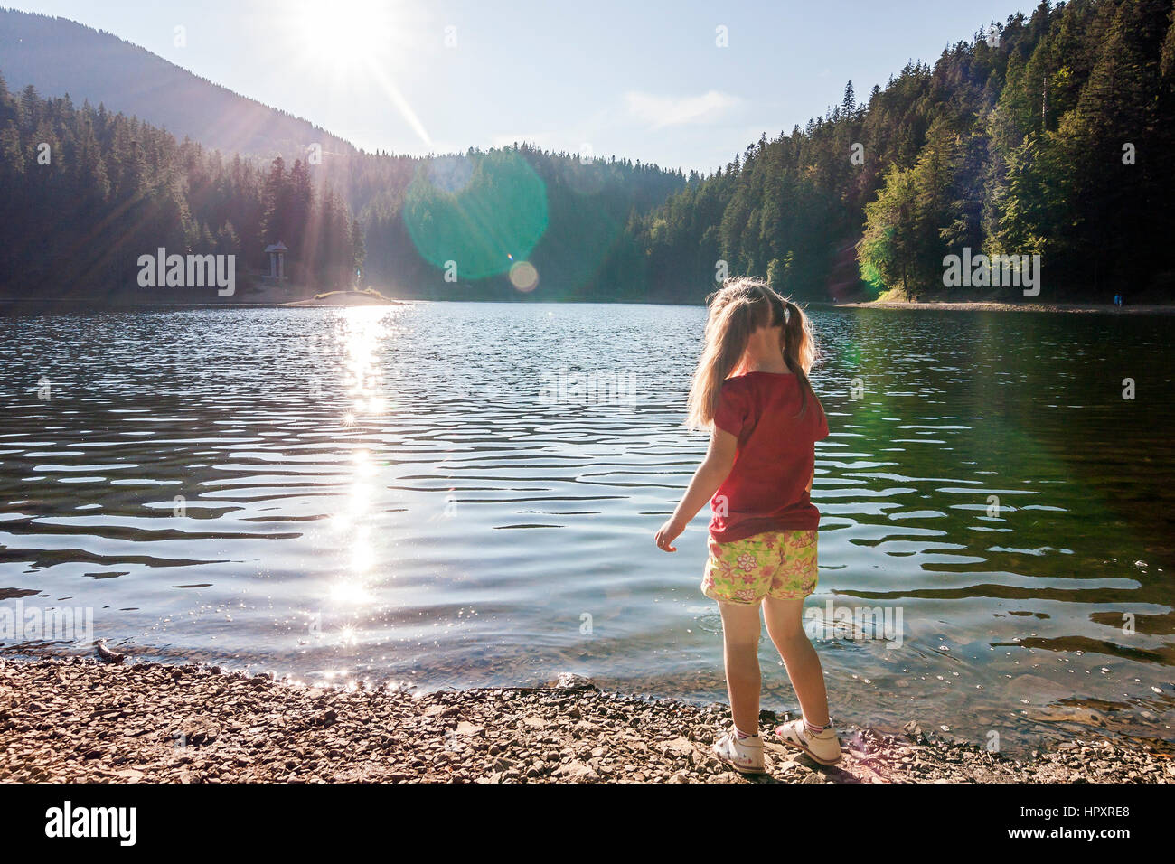 A cute little girl plaing on the bank of a mountain lake on a warm ...