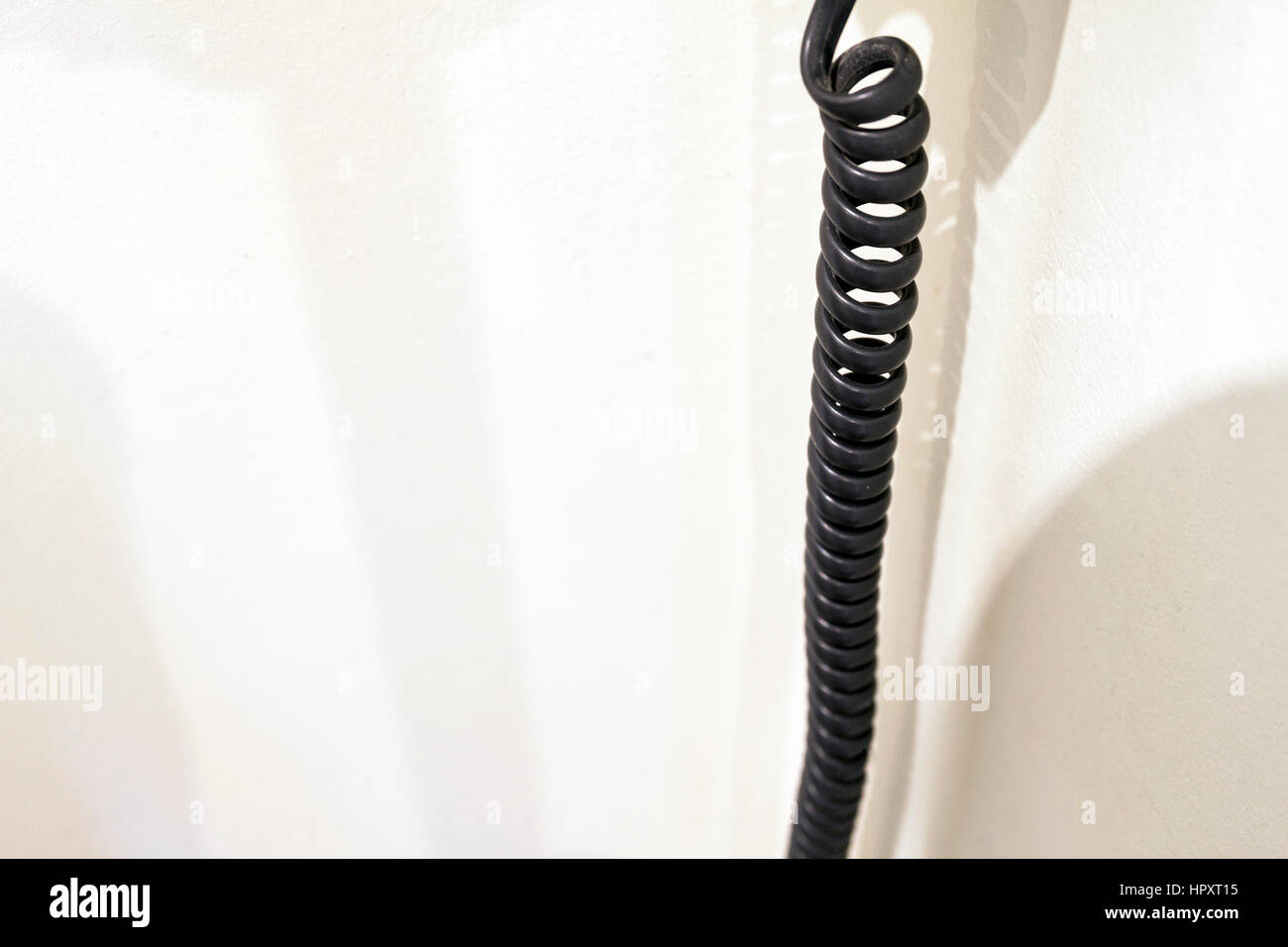 Spiral black spring telephone cable on white wall Stock Photo - Alamy