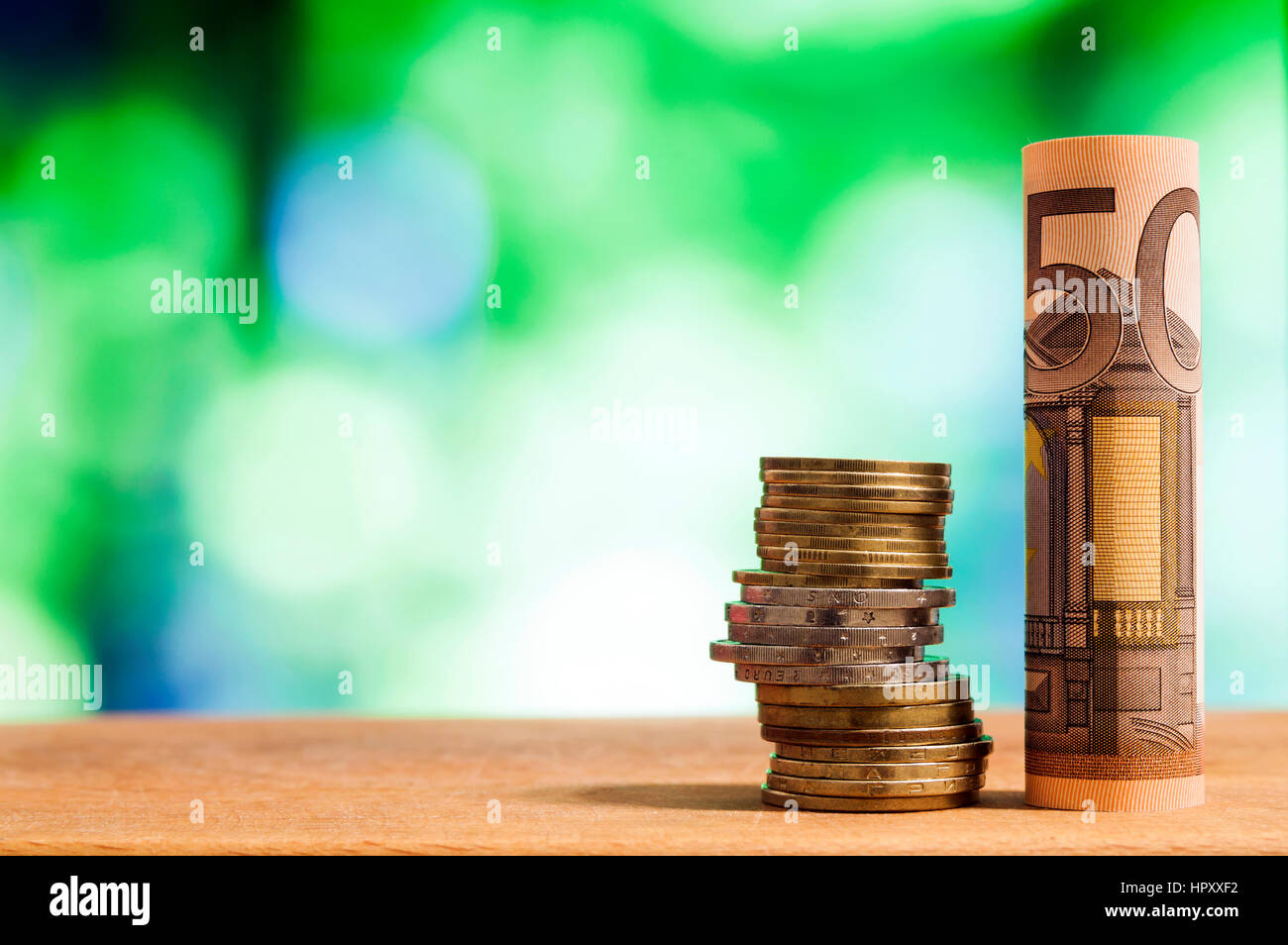Fifty euro rolled bill banknote, with euro coins on green blurred bokeh ...