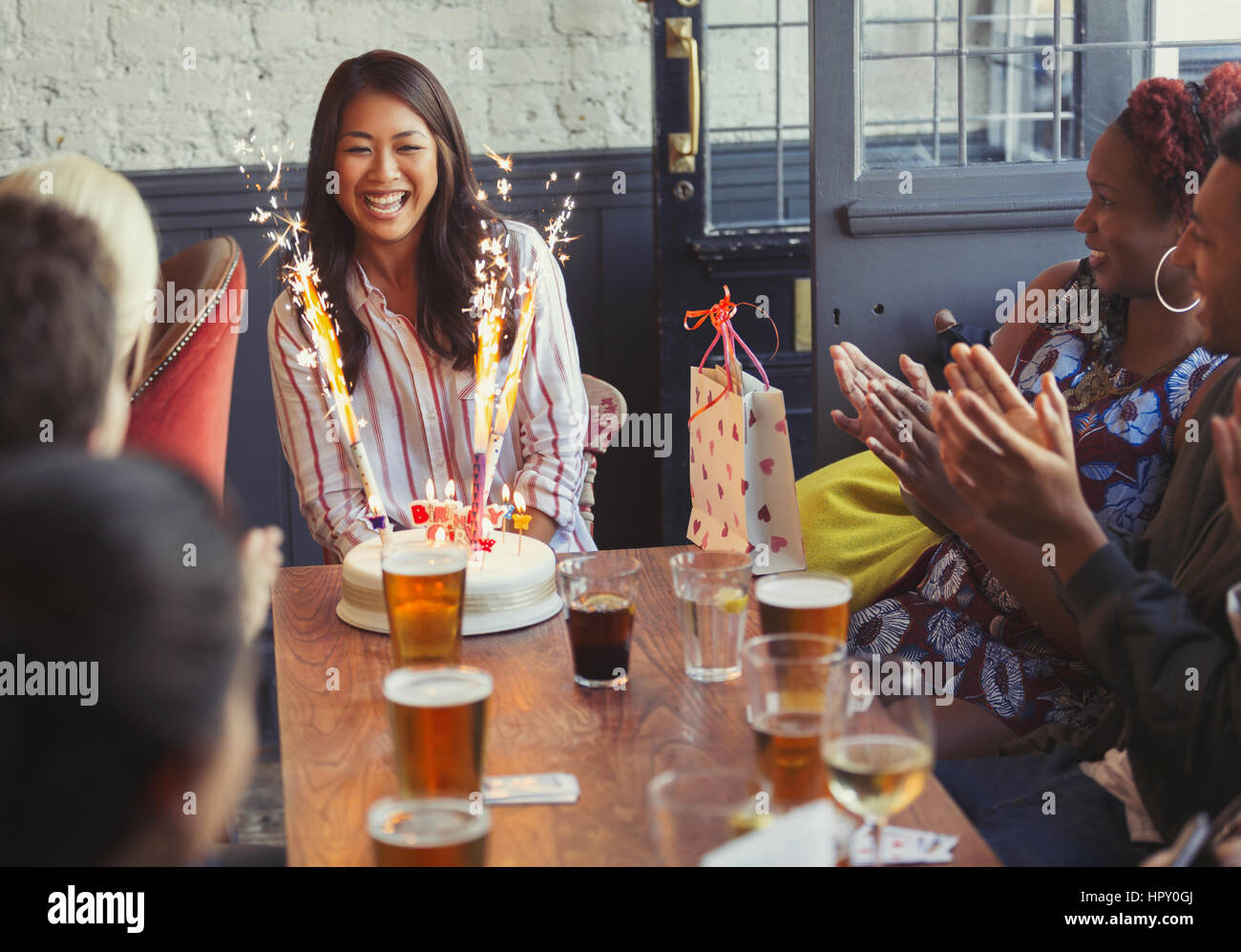 Friends clapping for happy woman with fireworks birthday cake at ...