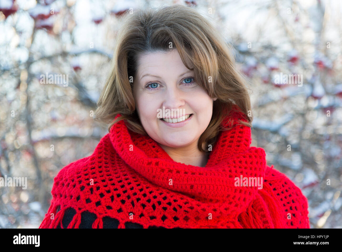 A woman in a red shawl in the winter is on the background of viburnum ...