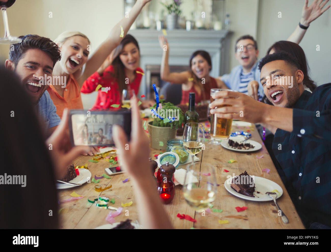 Woman with camera phone photographing playful friends throwing confetti ...