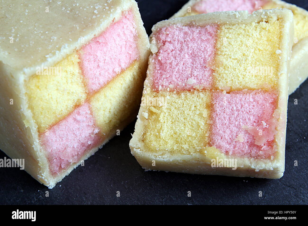 Freshly cut Battenberg Cake on dark slate board. Pink and yellow sponge ...