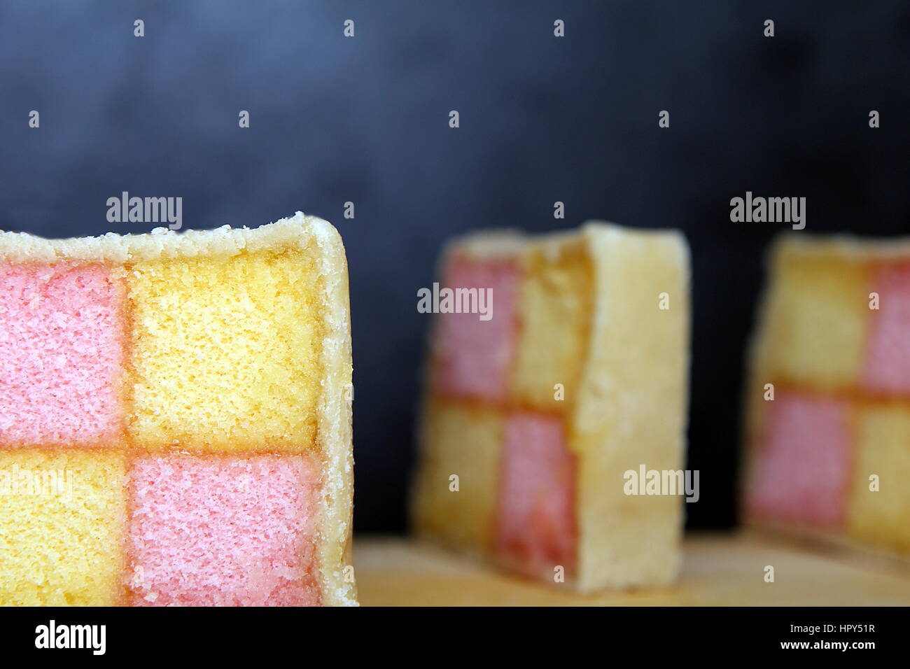 Freshly cut Battenberg Cake slices on wooden board with dark background ...