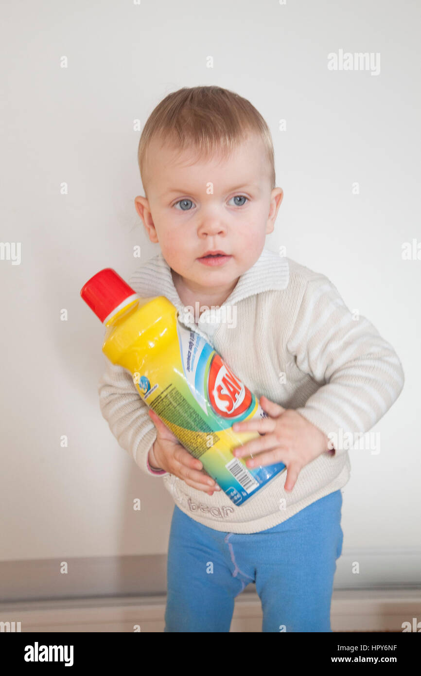 Little child playing with cleaning products at home on white background ...