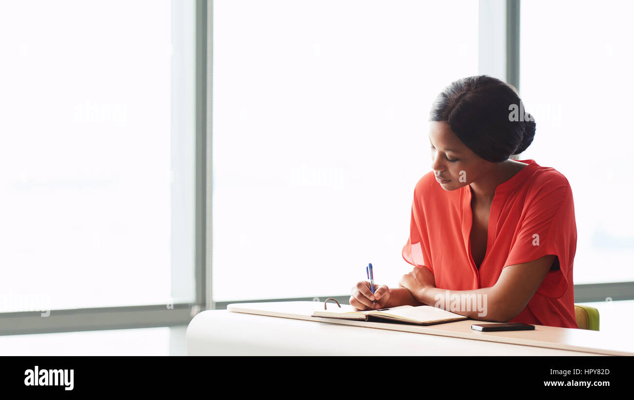 Adult female African writer busy writing in her notebook while wearing ...