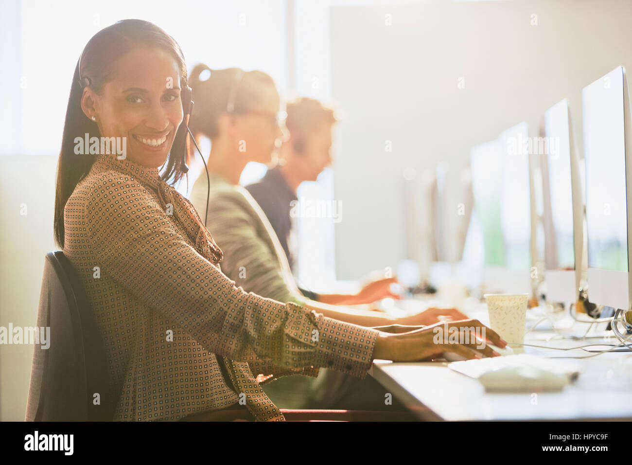 Portrait smiling female telemarketer wearing headset at computer in ...