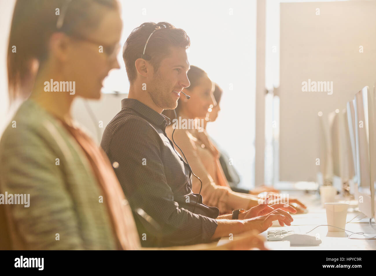 Telemarketers wearing headsets talking on telephone and working at ...