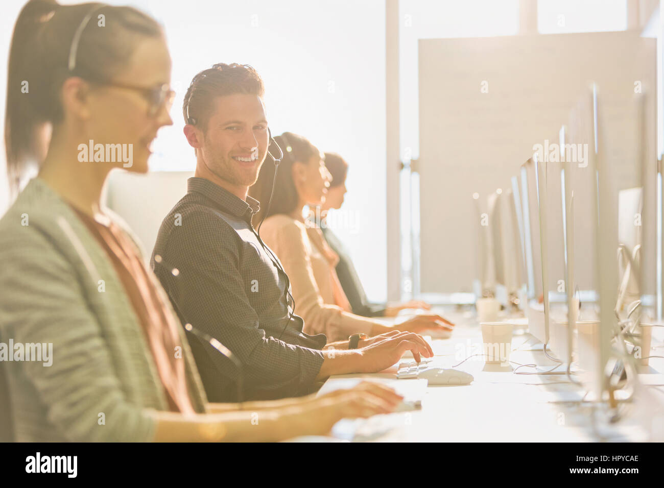 Portrait smiling male telemarketer wearing headset at computer in sunny ...