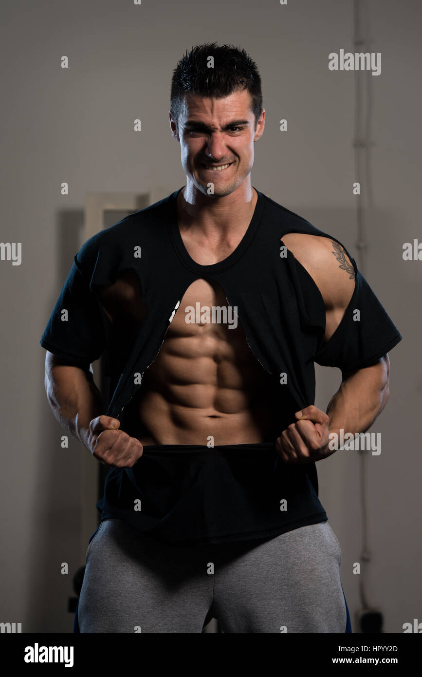 Handsome Man Standing Strong In The Gym And Ripping the T-Shirt Off ...