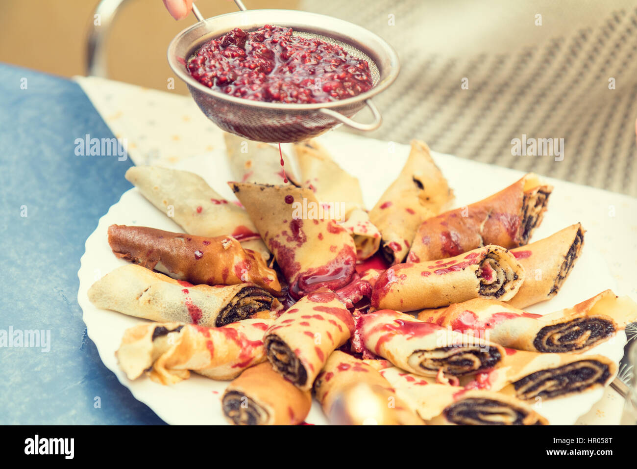 Crepes filled with poppy on white plate. Spring rolls. Woman pouring ...