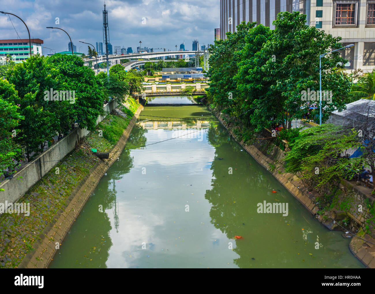 a river in the middle Jakarta near Central Park Mall with reflection of buildings and trees ...