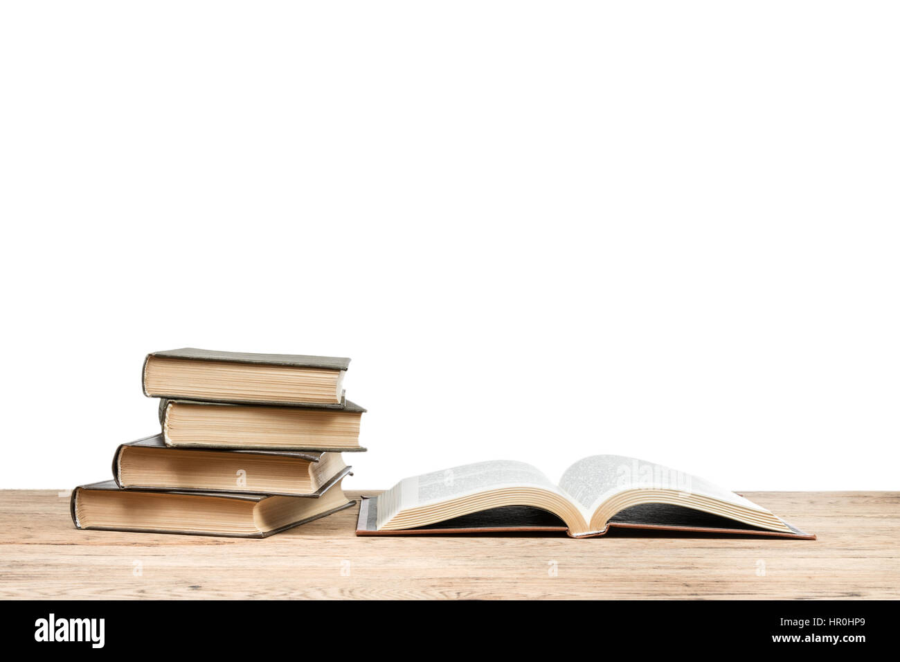 Open book near the pile of books lying on a wooden table isolated on ...