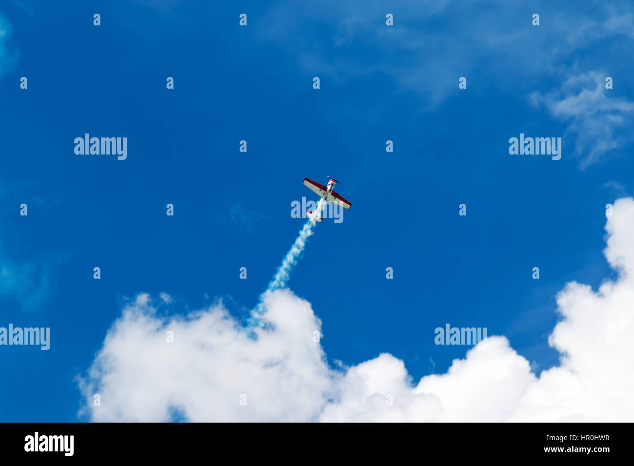 Red and white sport plane flies up releasing a stream of smoke into the ...