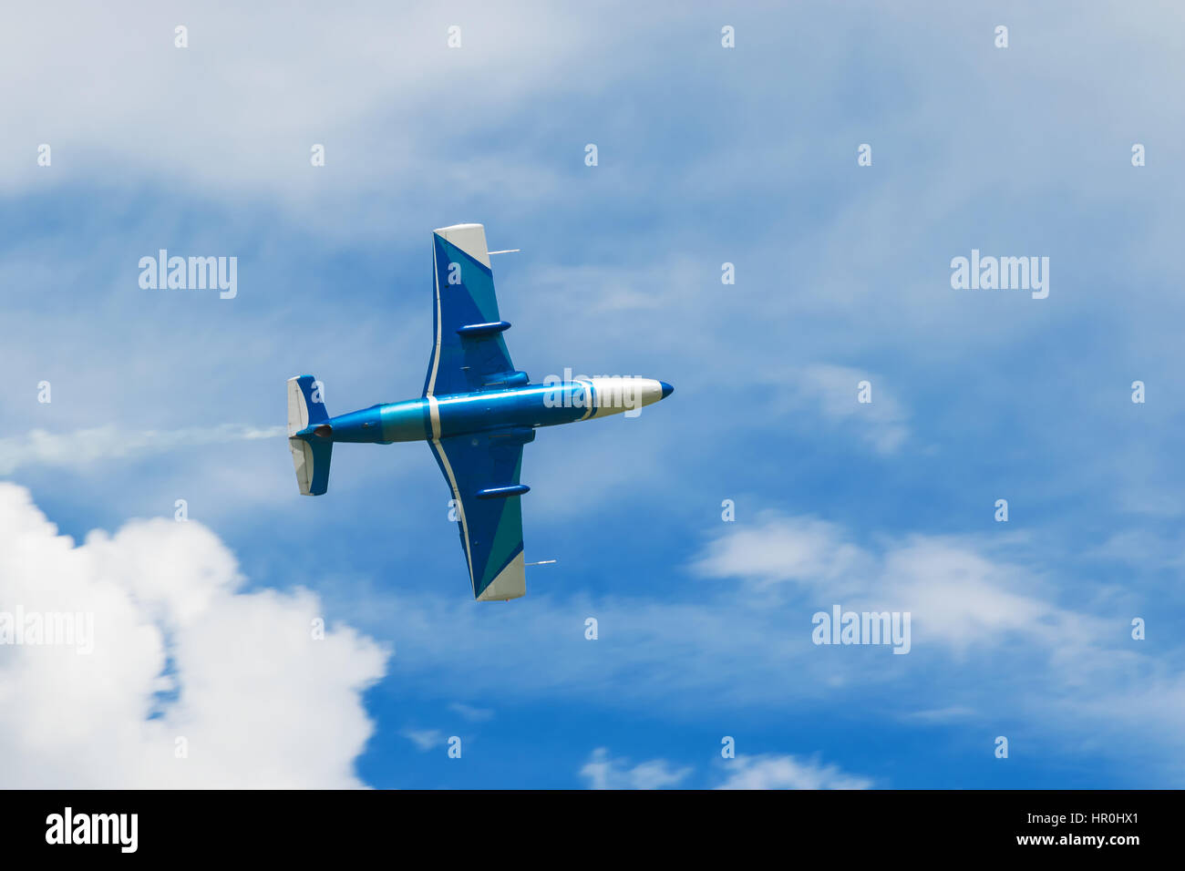 Blue jet plane jetting smoke flying in the blue sky with clouds closeup ...