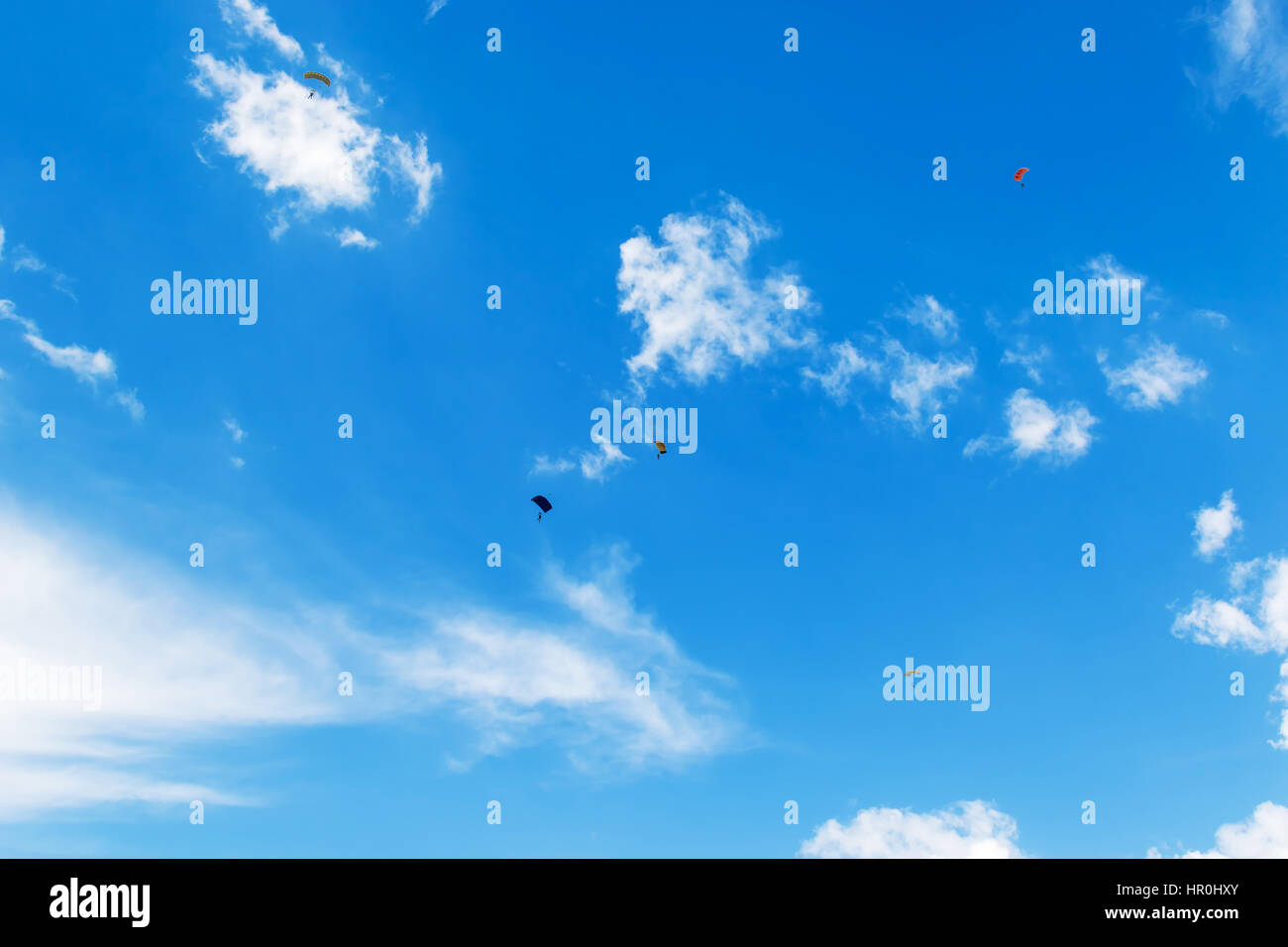 Five skydivers with open parachutes floating in the blue sky with ...