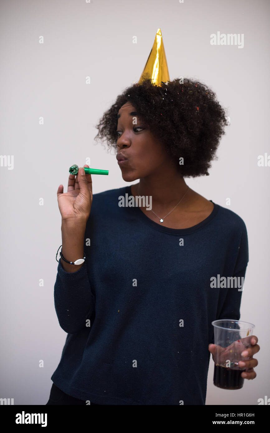portrait of a young beautiful black woman in party hat blowing in ...