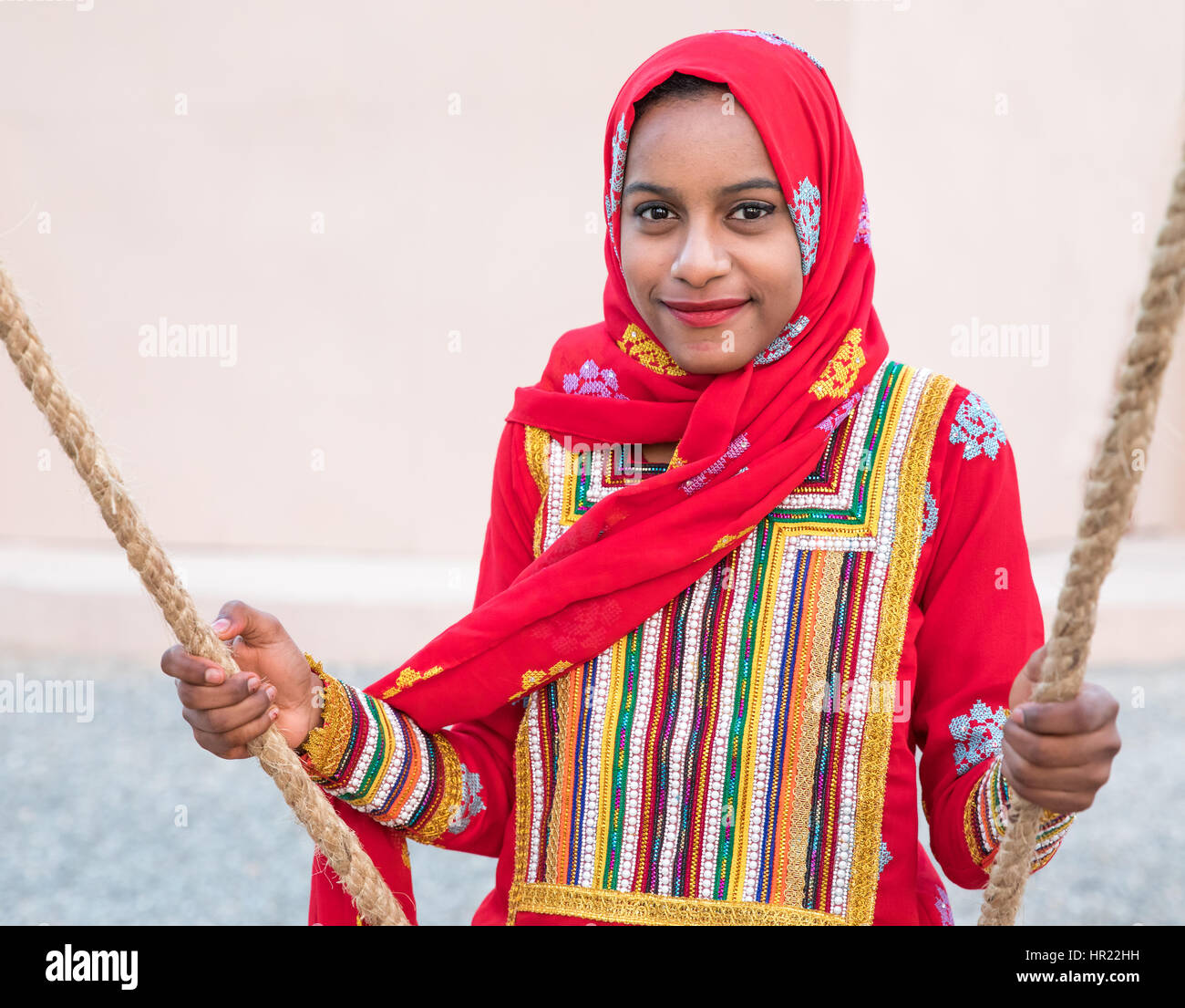 Young Omani girl in a red traditional dress sitting on a swing Stock ...