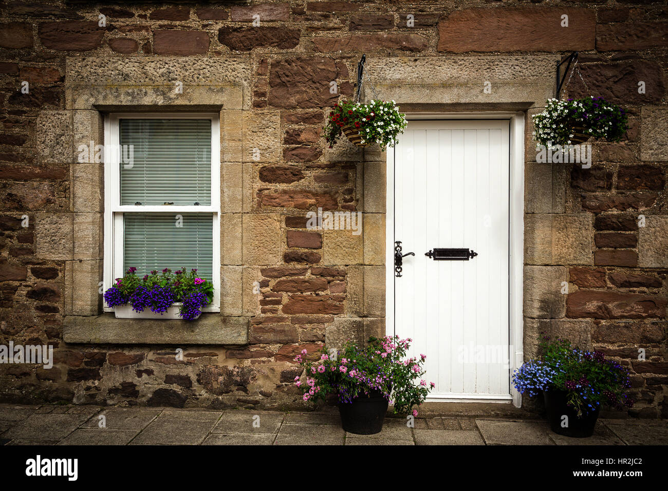 Door and window detail of a stone cottage facade, with hanging baskets ...
