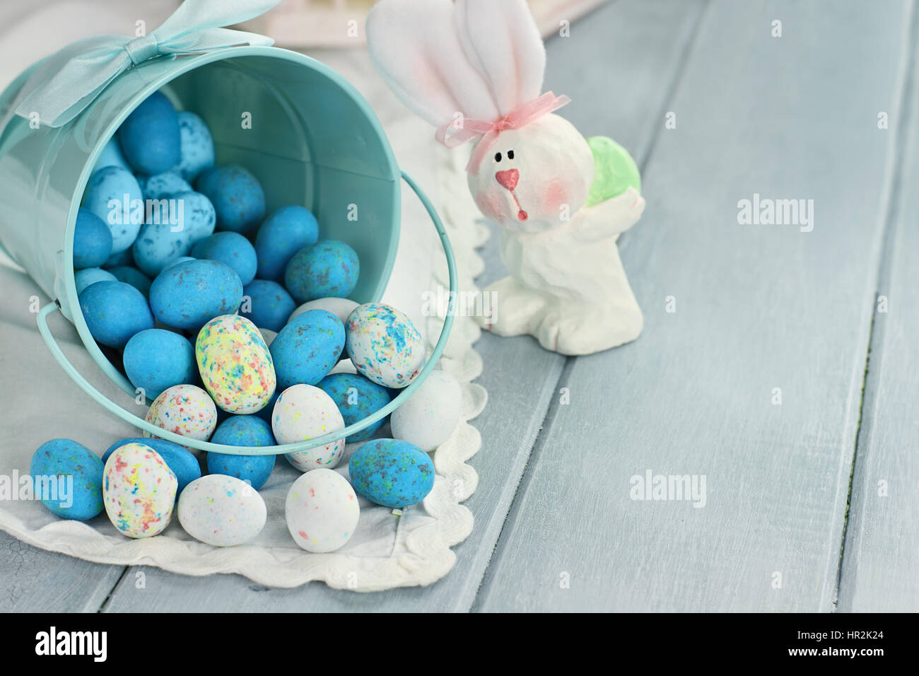 A blue tin bucket tipped over, spilling Easter candy eggs onto a table ...