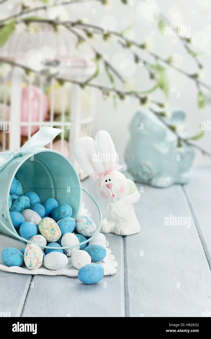 A blue tin bucket tipped over, spilling Easter candy eggs onto a table ...