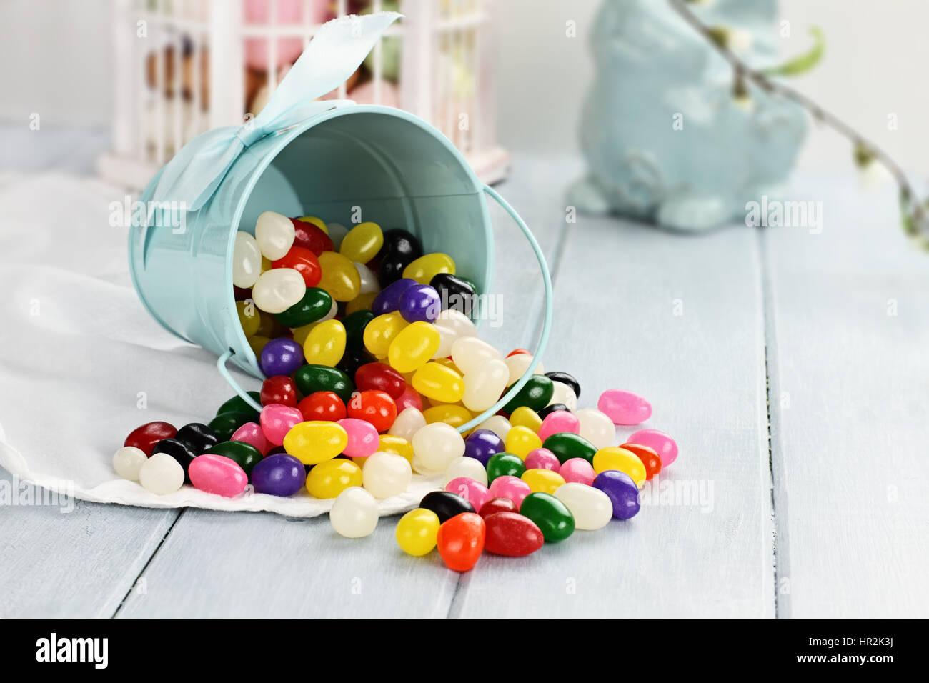 A blue tin bucket tipped over, spilling jelly beans onto a table ...
