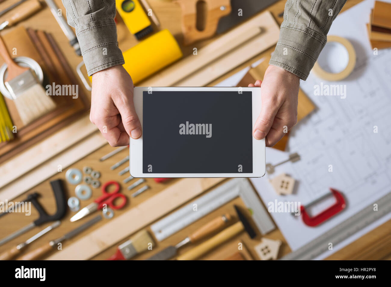 Male hands holding a digital tablet, work table with tools and project ...