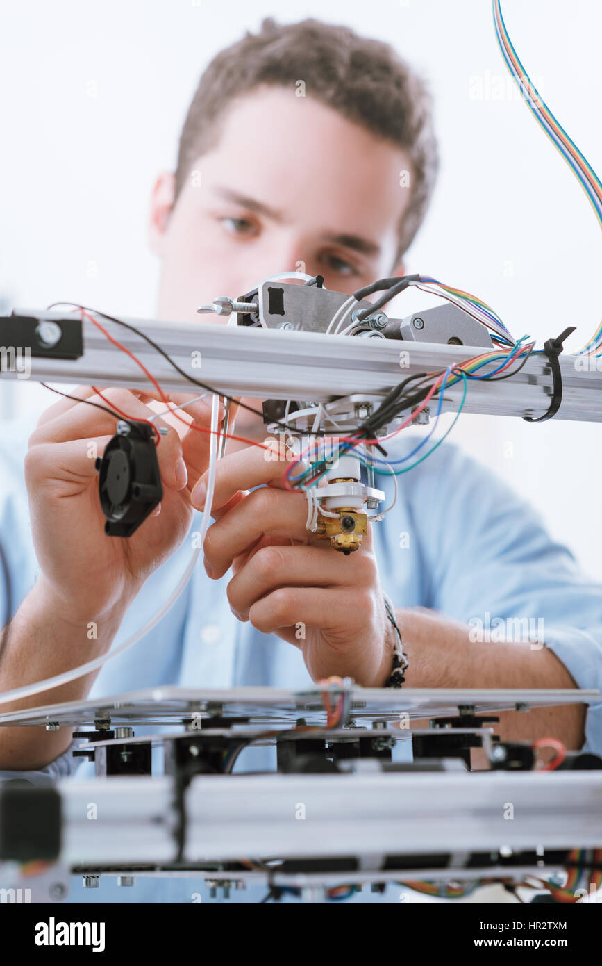 Young engineer in the laboratory working on a 3D printer and checking ...