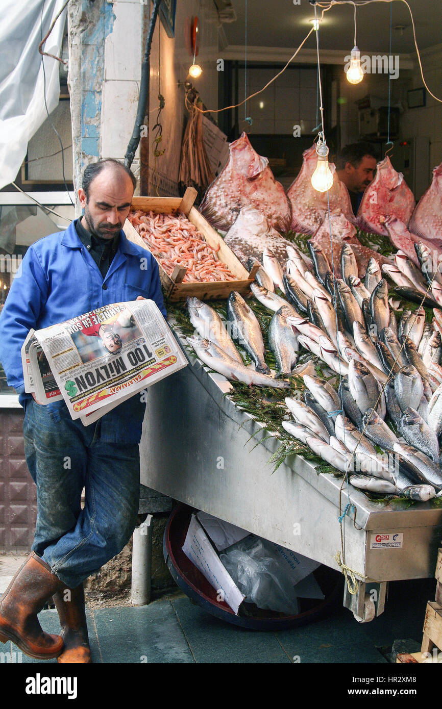 Fishmonger at a fish stall in a market reads a newspaper. Photographed ...