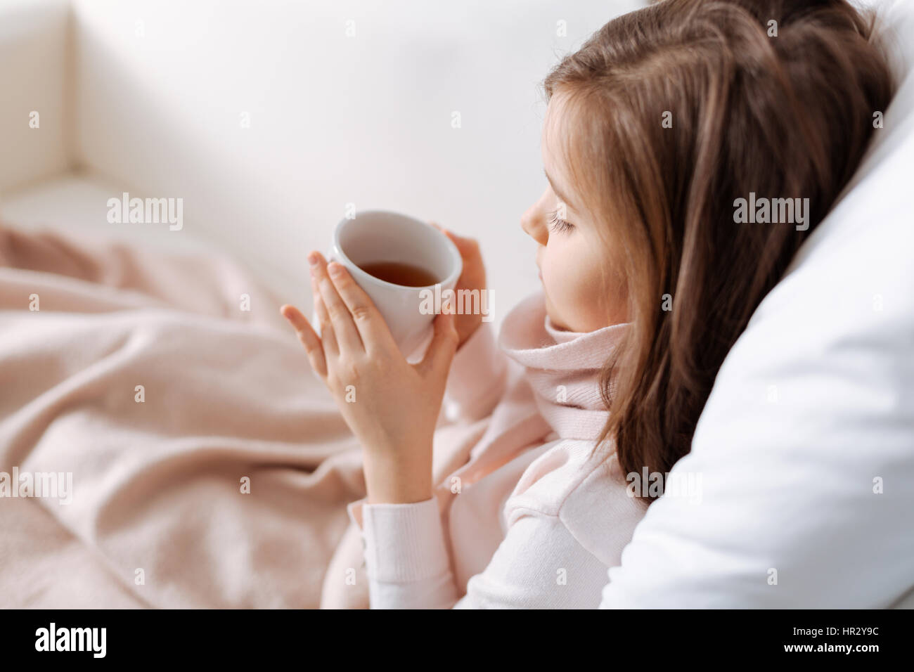 So warm. Pleasant tired little girl drinking tea and resting at home ...