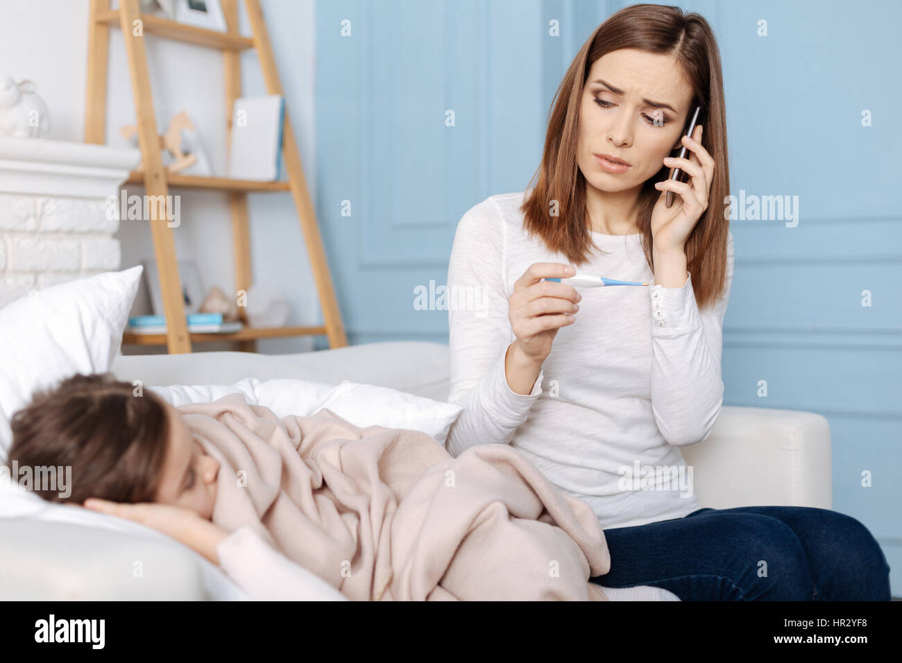 We need help. Pleasant caring mother calling a doctor while her sick ...