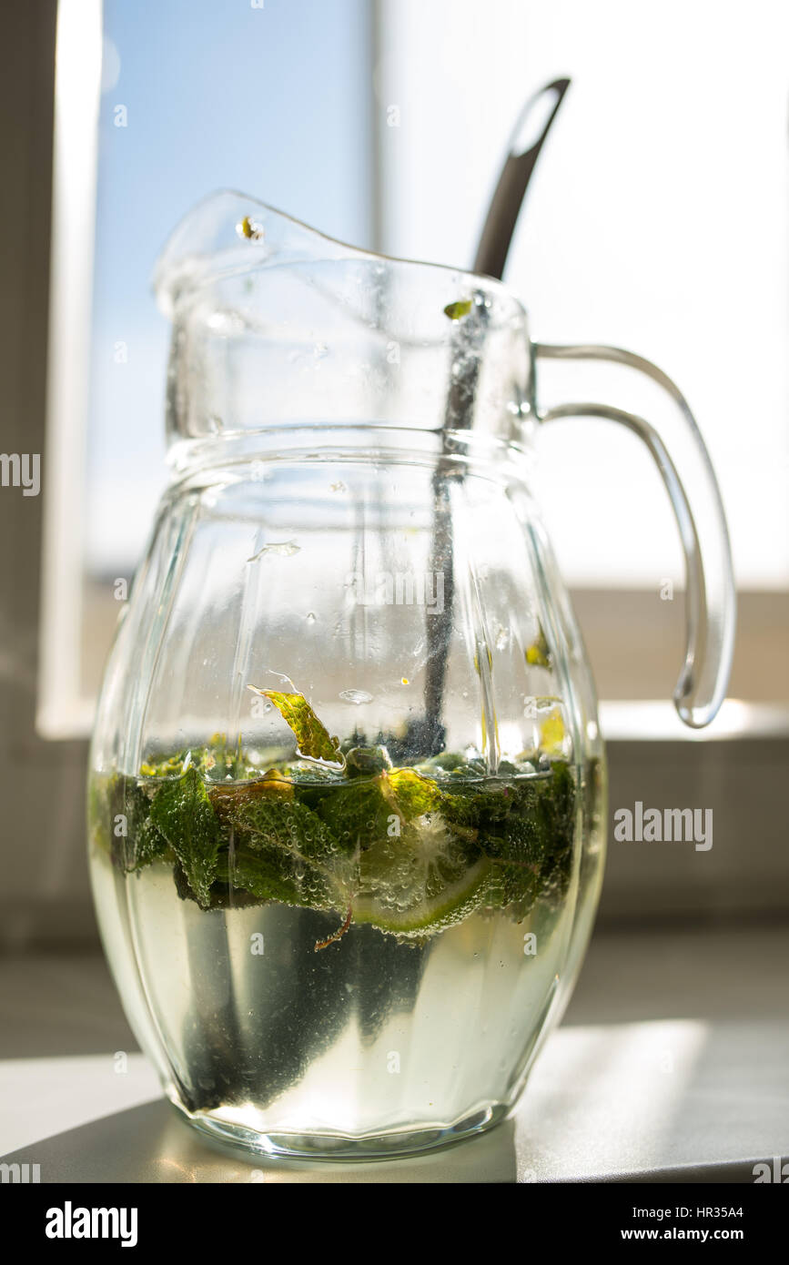 Carbonated soda water or juice with lime and mint in a glass jug on the ...