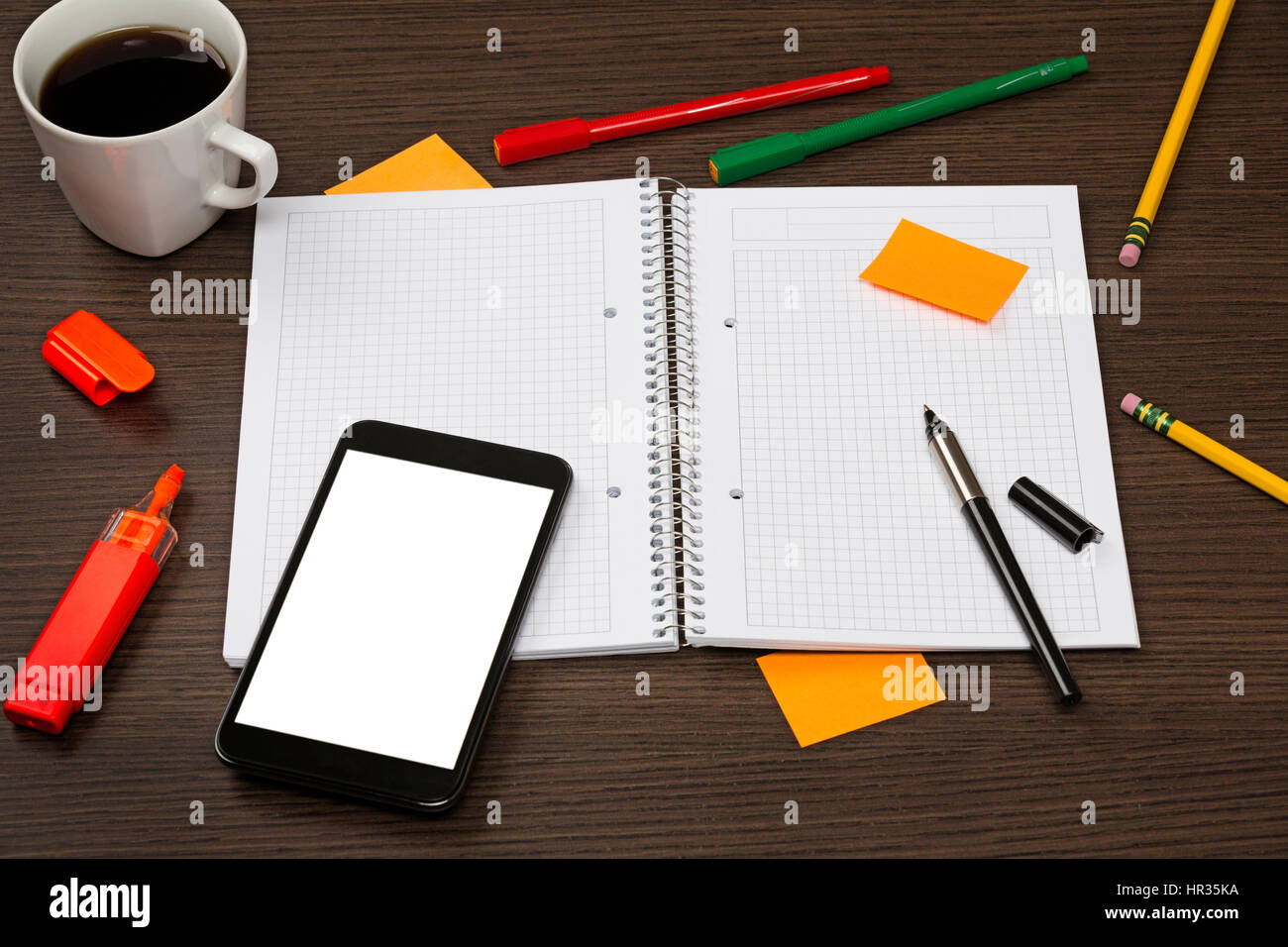 Opened notebook, smartphone with blank screen, pen, sticky note, cup of ...