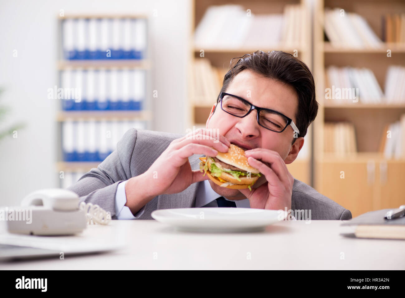 Hungry funny businessman eating junk food sandwich Stock Photo - Alamy