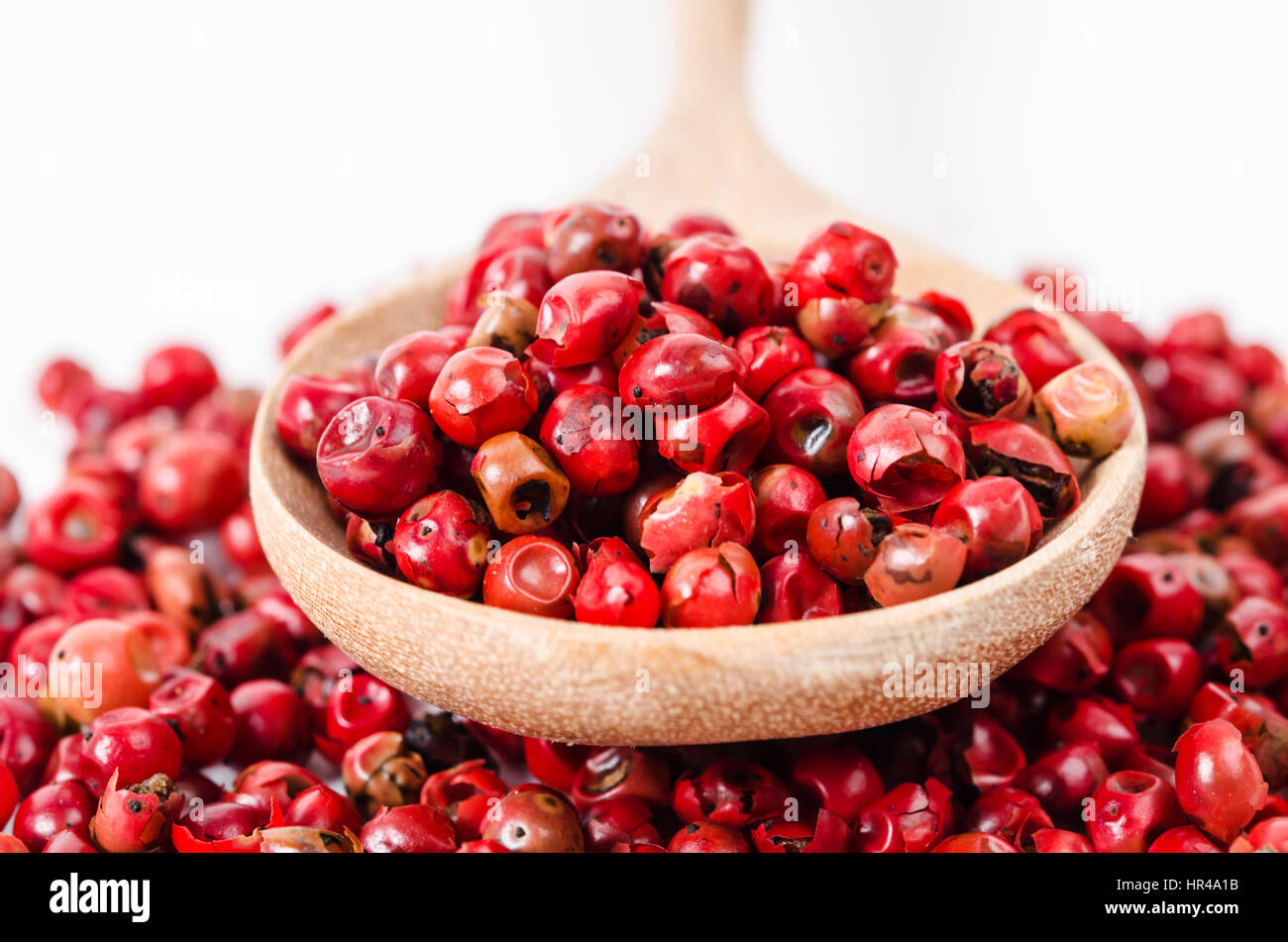 Wooden spoon filled with dried pink pepper berries on white background ...