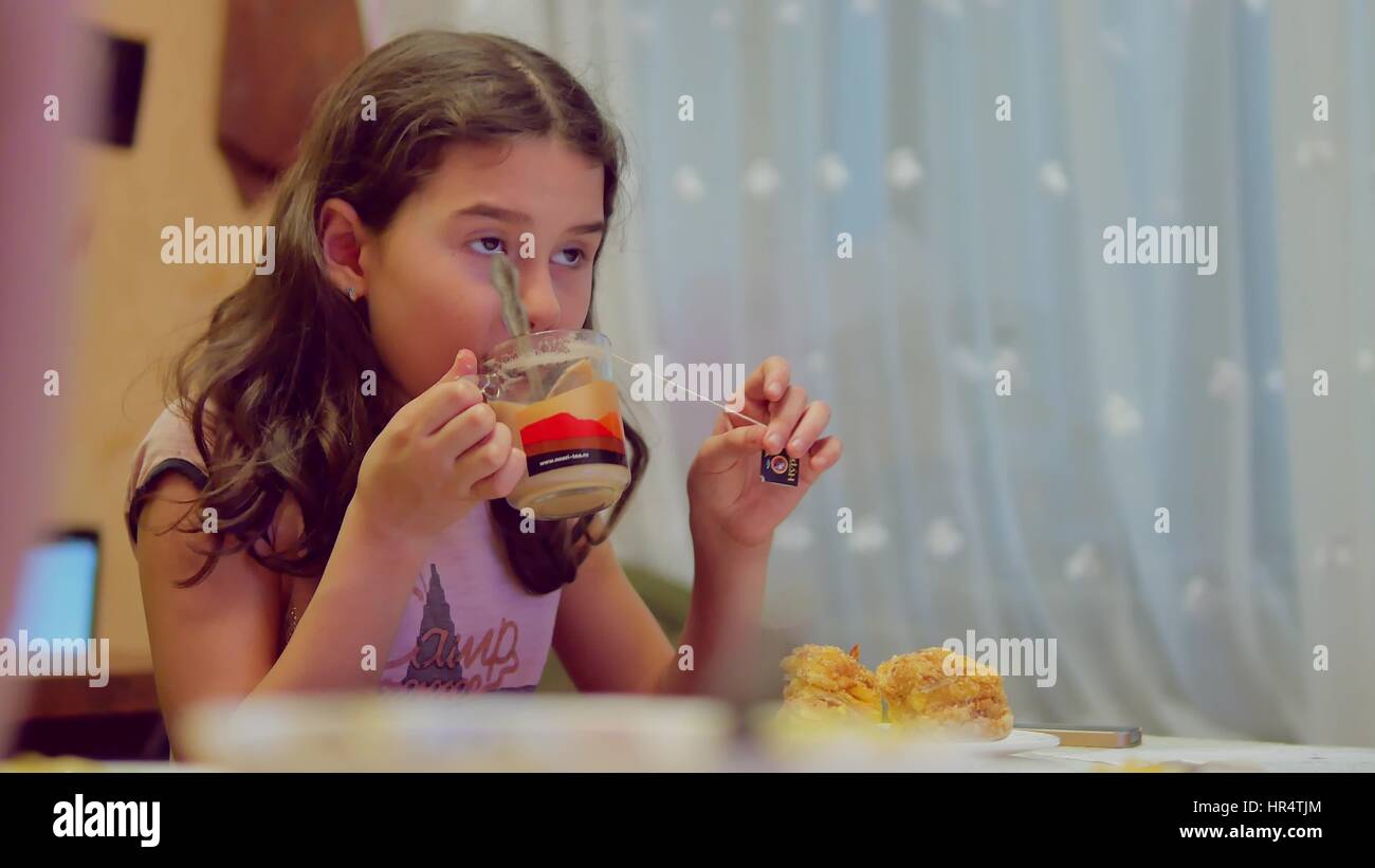 teen girl drinking the tea and eating cake, indoor lifestyle watching ...