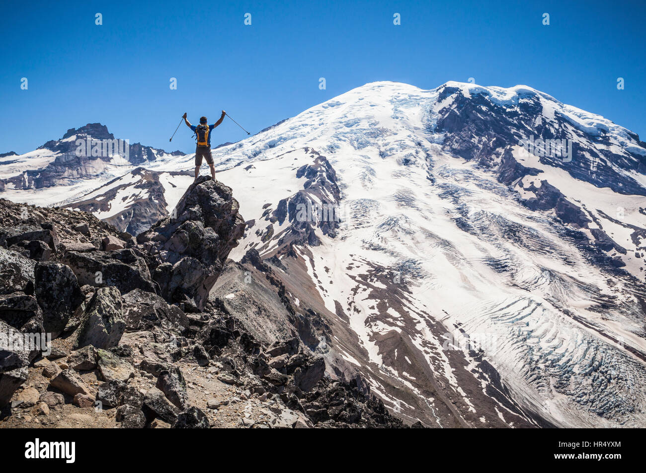 A man giving the upraised arms victory sign atop a rocky outcrop with ...