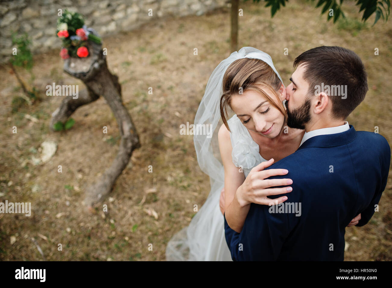 Groom kissing bride on neck background wooden stump with wedding ...