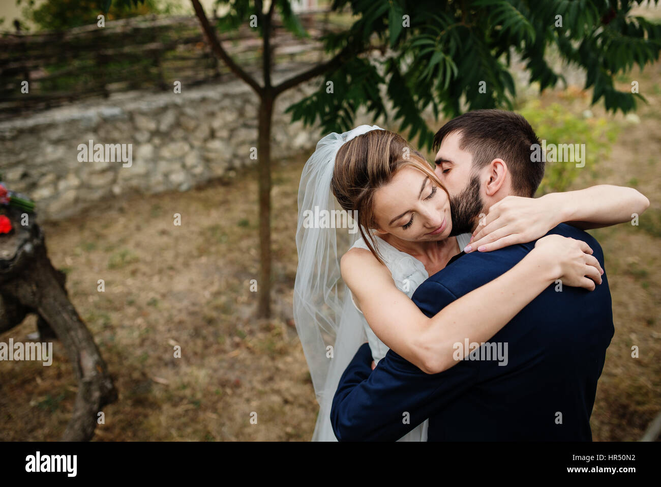 Groom kissing bride on neck background wooden stump with wedding ...