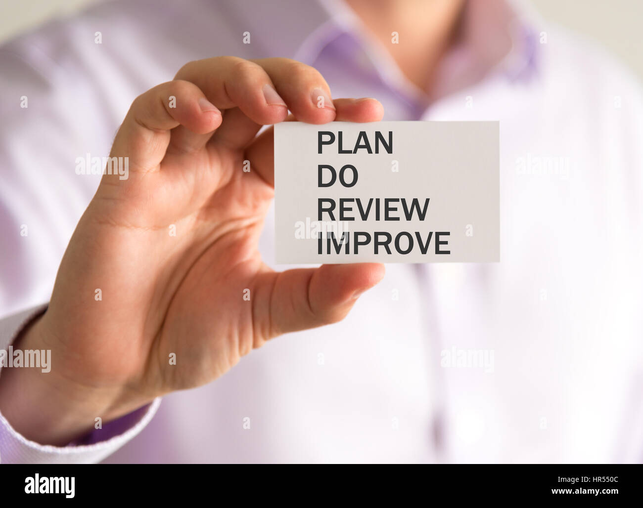 Closeup on businessman holding a card with PLAN DO REVIEW IMPROVE ...