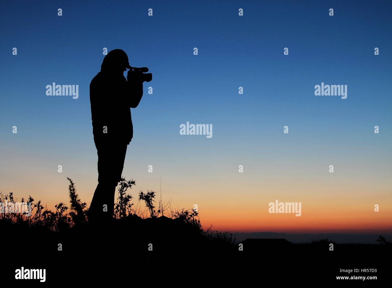 Silhouetted man standing in sunset on mountain with camcorder Stock ...