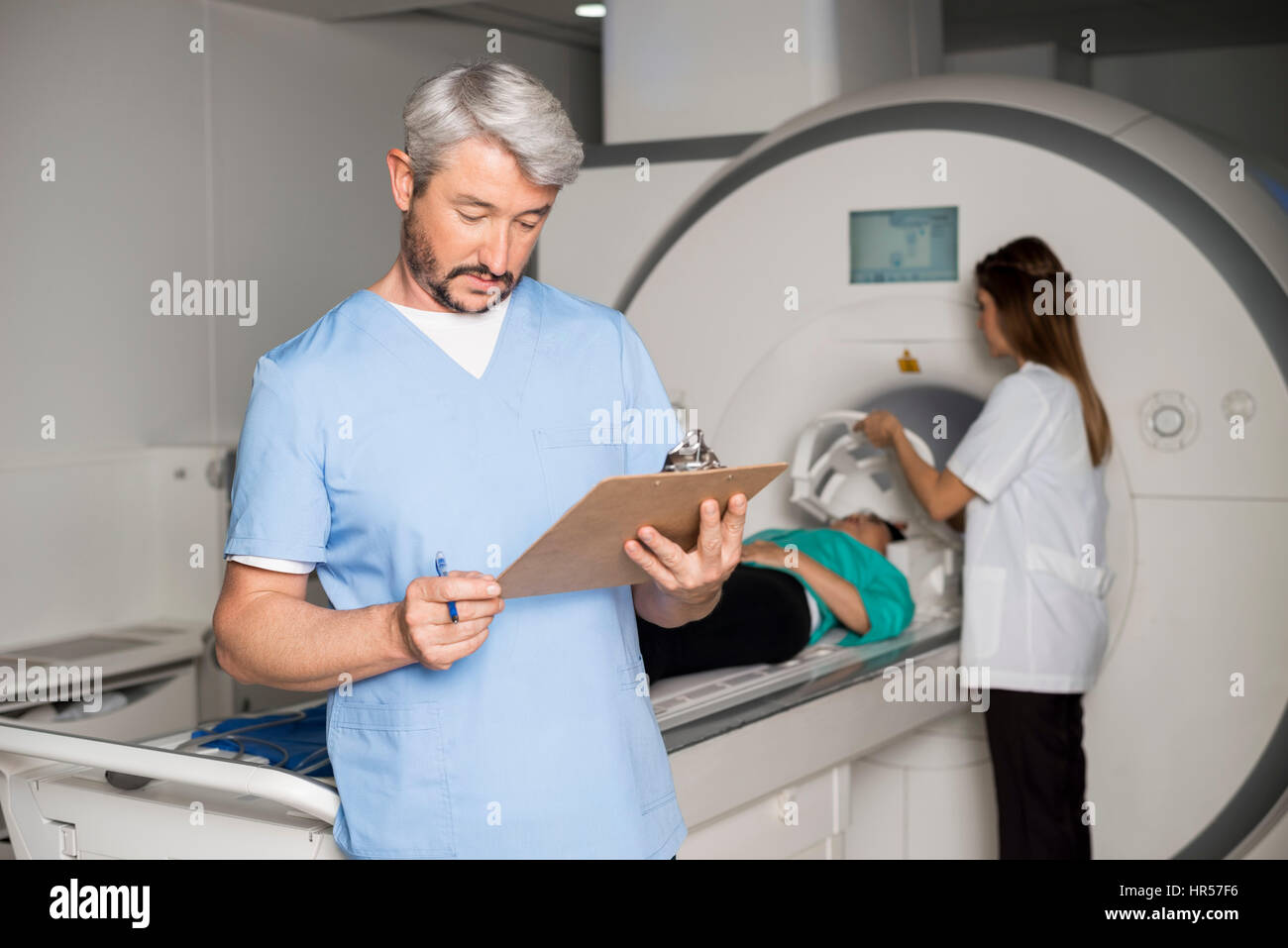 Male doctor reading clipboard with female colleague preparing patient ...