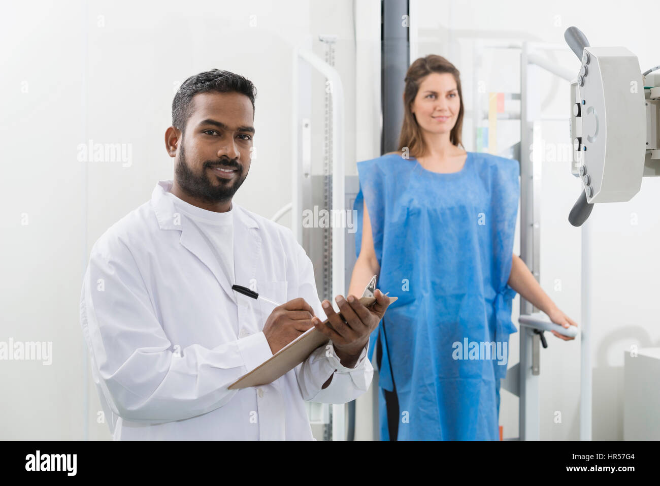 Portrait of male radiologist writing on clipboard with patient ...