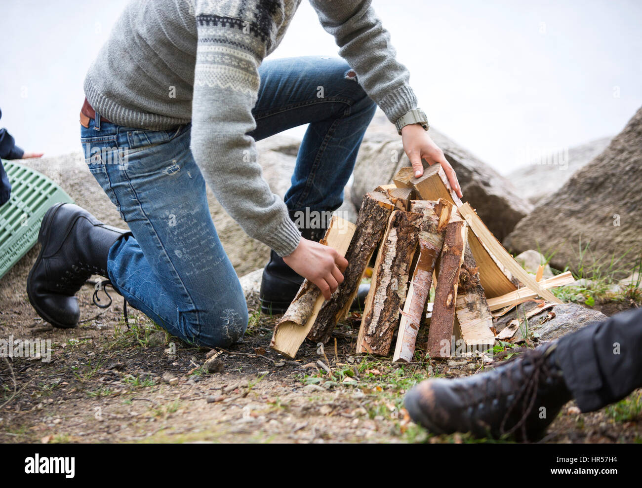 Low section of young man arranging firewood for bonfire on lakeside ...