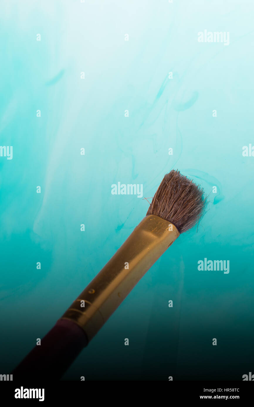 Watercolor paint dissolving in water as painting brush touches water ...