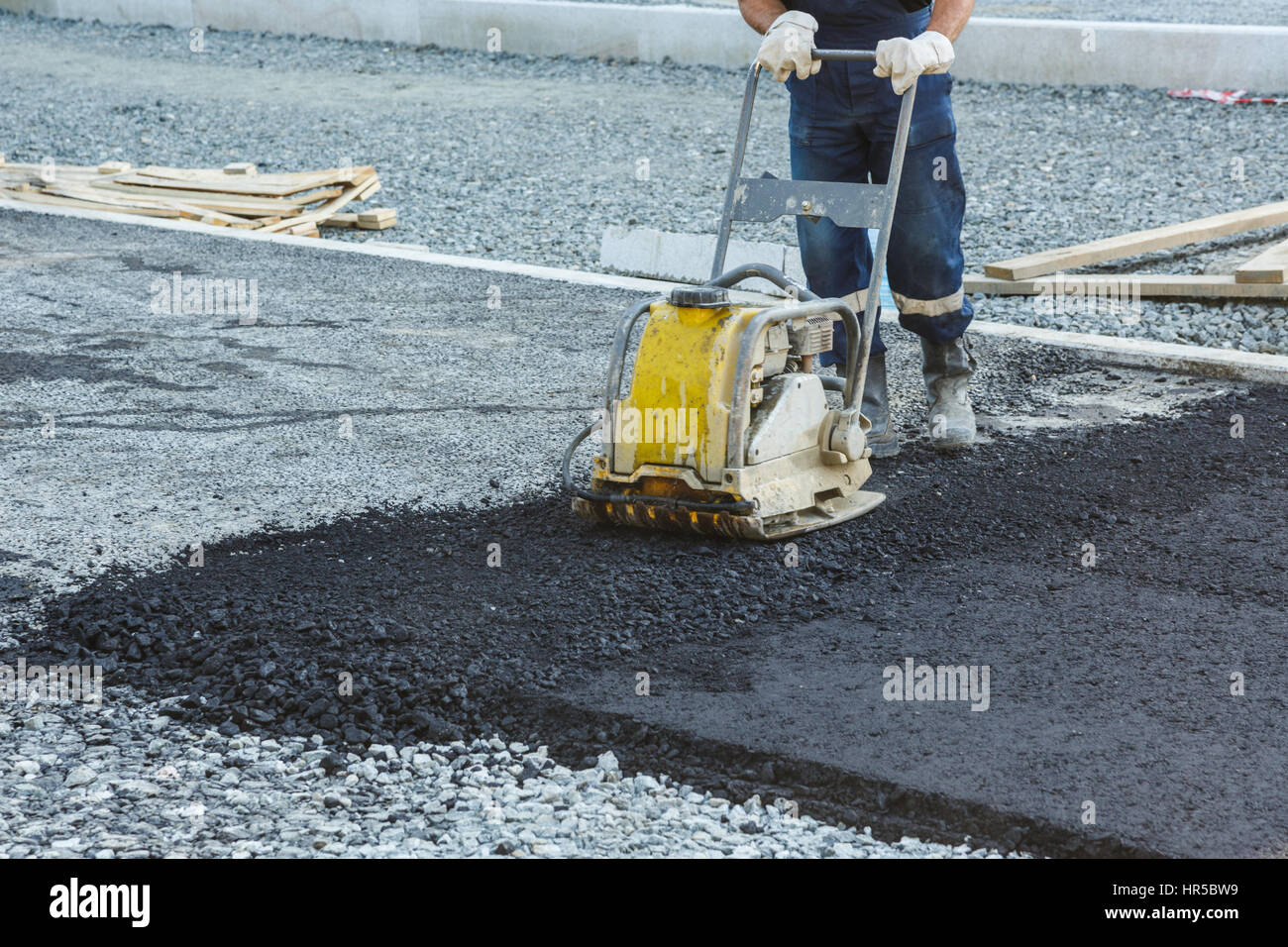 Worker use vibratory plate compactor compacting asphalt at road repair ...