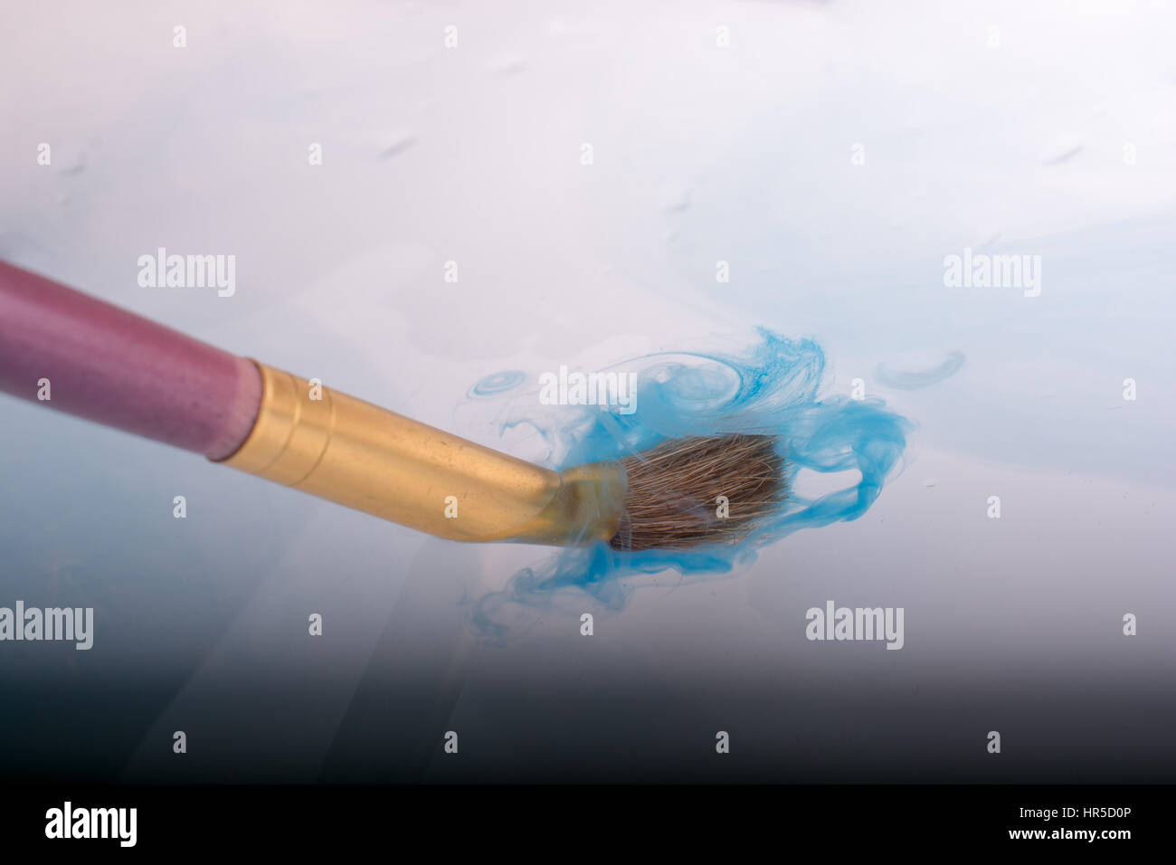 Watercolor paint dissolving in water as painting brush touches water ...